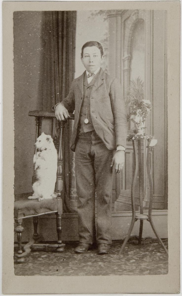 Studio portrait of standing man, with dog begging on chair - AGSA ...