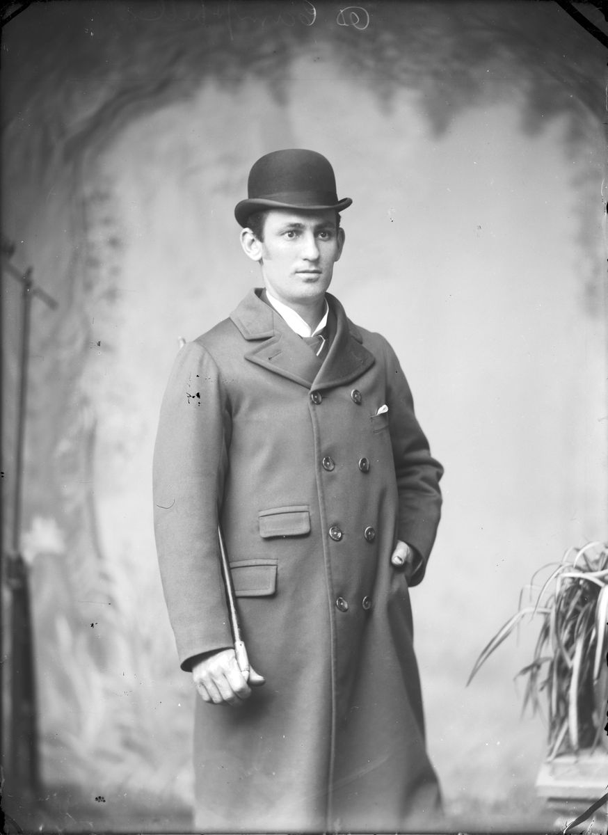 Studio portrait of young man wearing bowler hat, hand in jacket pocket ...